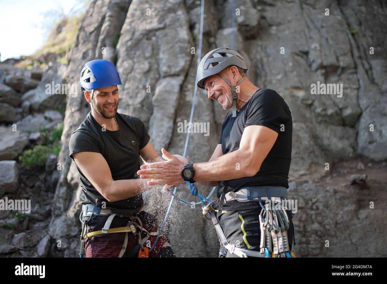 Senior man with instructor using chalk before climbing rocks outdoors ...
