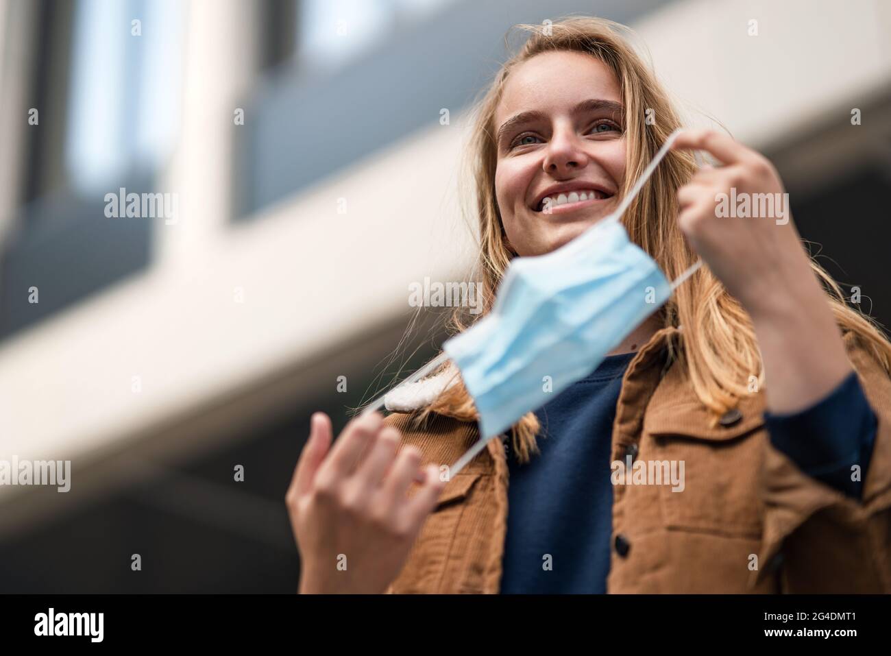 Portrait of young woman taking off face mask outdoors in city, life ...
