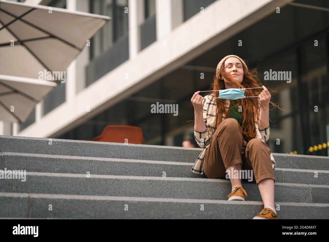 Portrait of young woman taking off face mask outdoors in city, life ...
