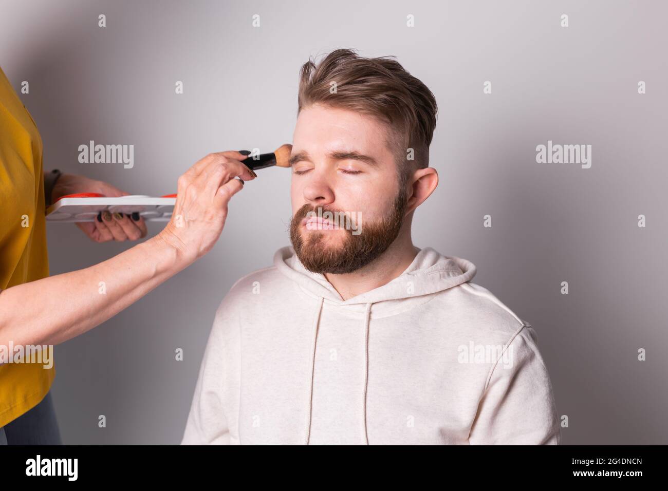 Professional make-up artist doing young man makeup in studio Stock ...