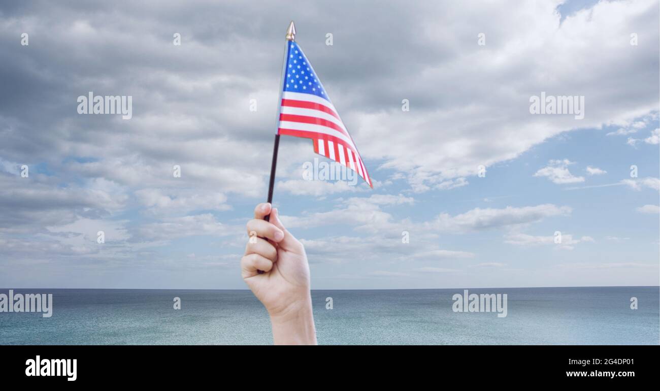 Composition of caucasian hand holding american flag over blue sky with ...