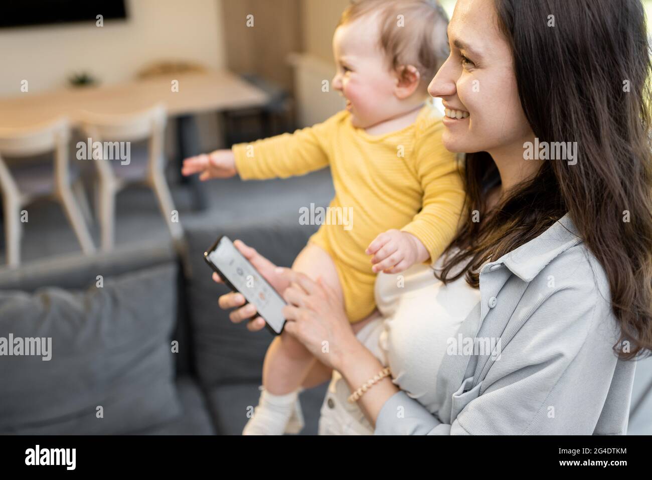 Mom controlling home devices by smartphone, standing with a baby at ...