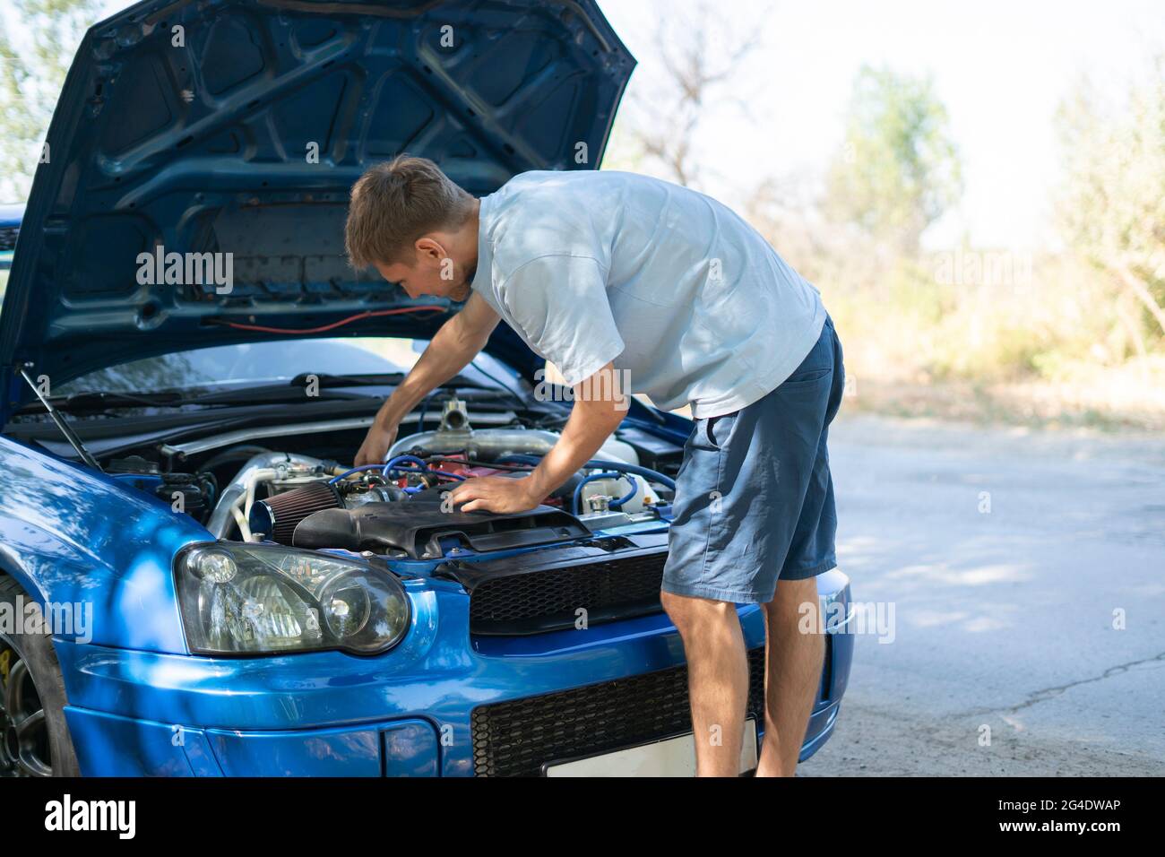 young man standing near the car with opened hood and fix some problems ...