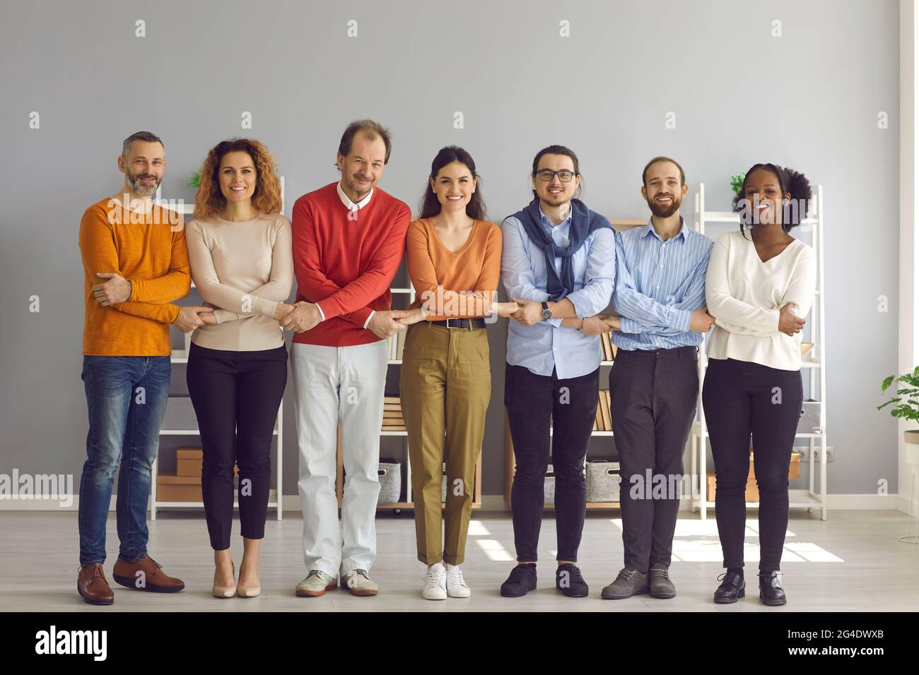 Diverse group of happy people standing in modern office, holding hands ...