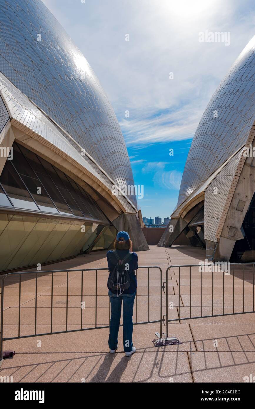 A woman takes photos of the Opera House shells with a phone from behind ...