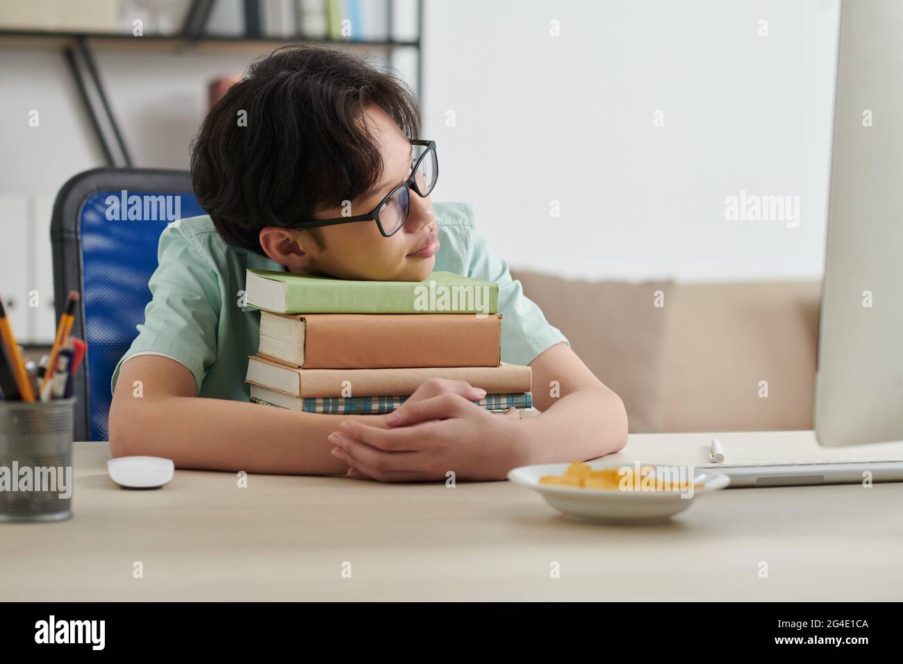 Dreaming teenage schoolboy in glasses leaning on stack of students ...