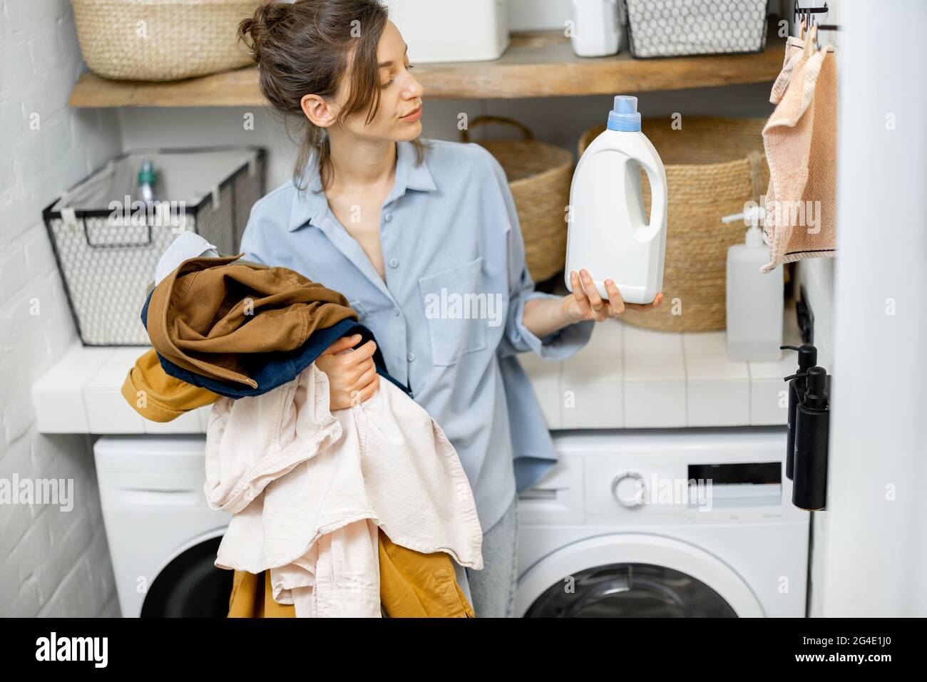 Woman with clean clothes and detergent in the laundry room at home ...