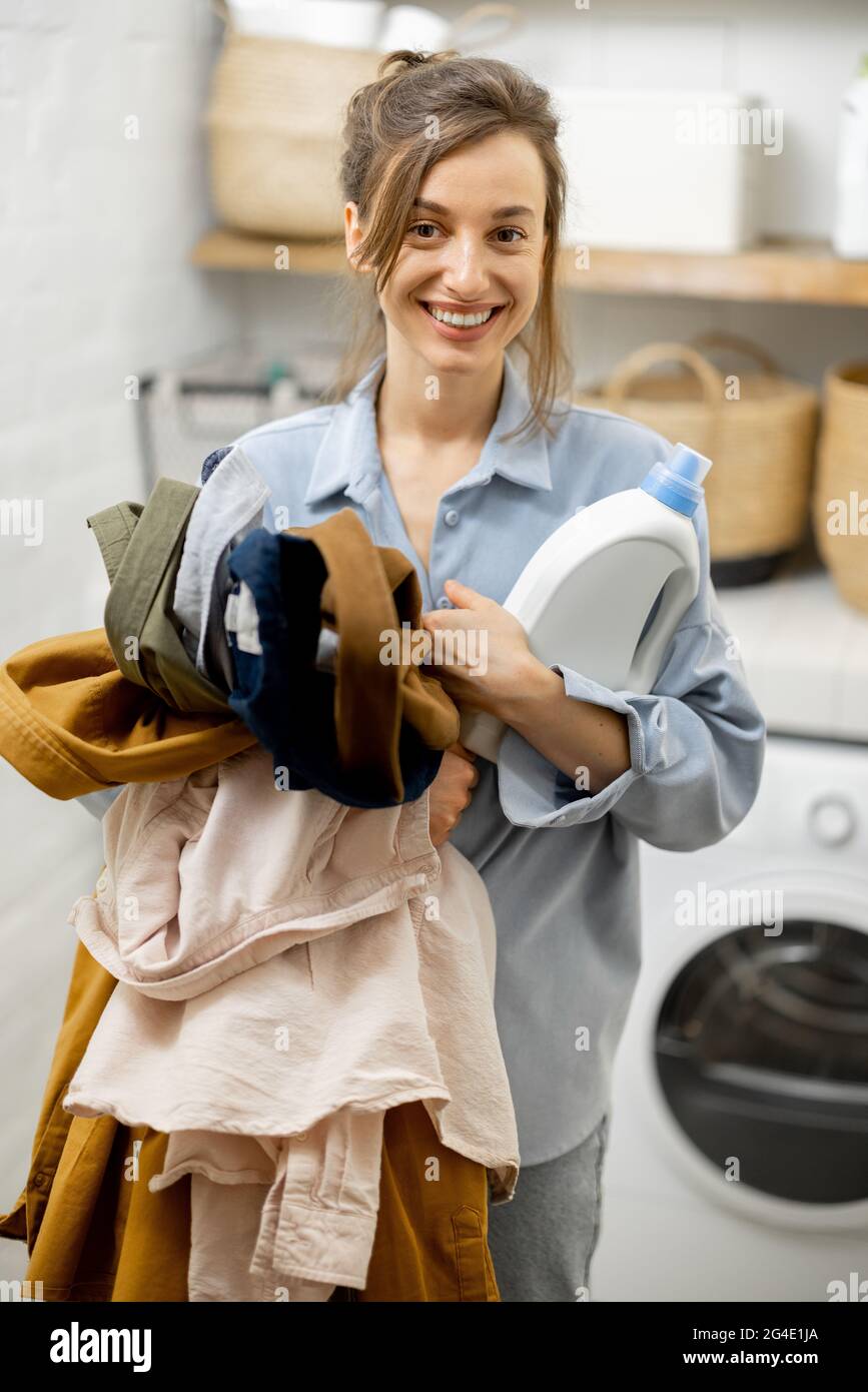 Woman with clean clothes and detergent in the laundry room at home ...