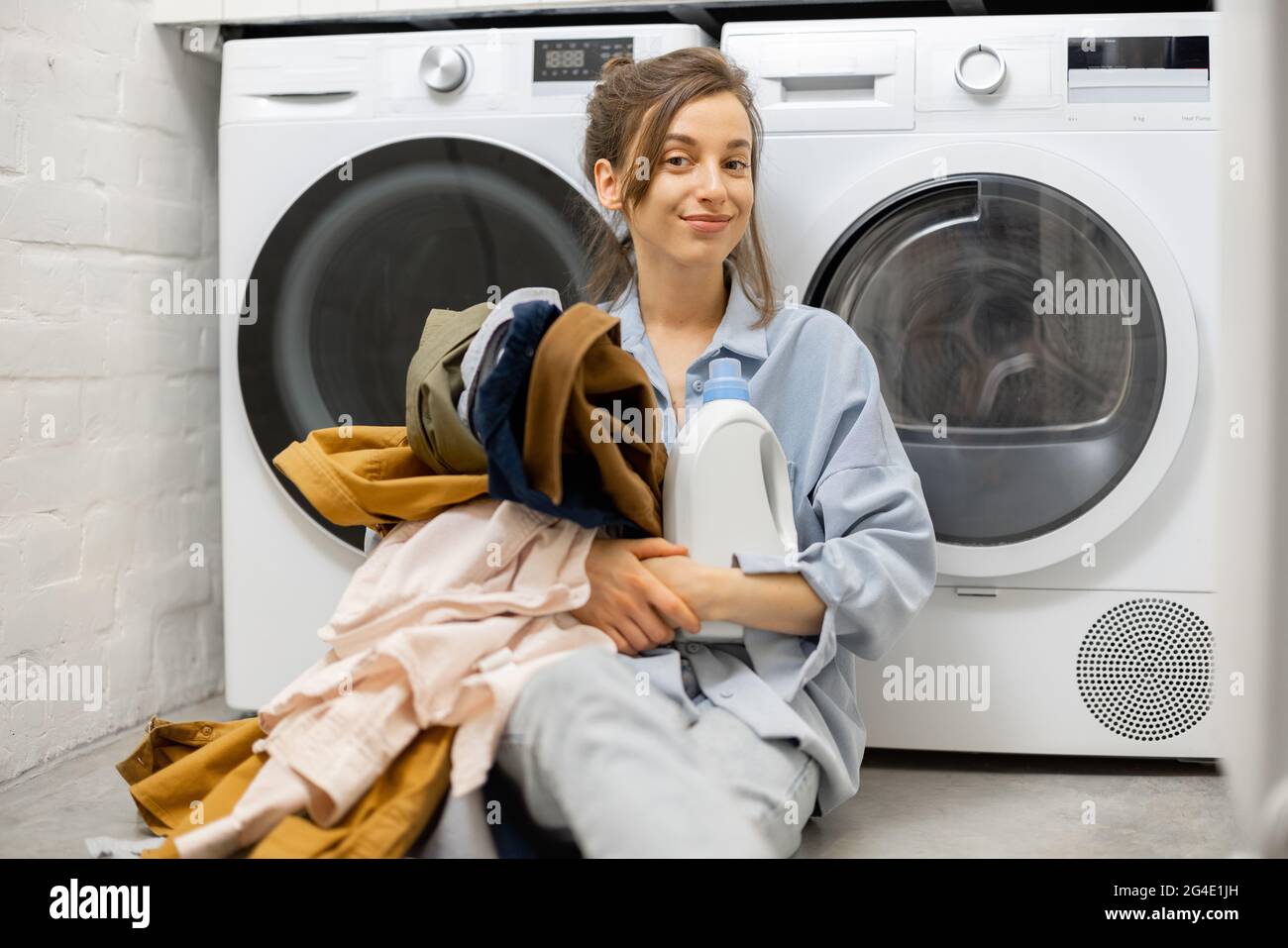 Woman with clean clothes and detergent in the laundry room at home ...