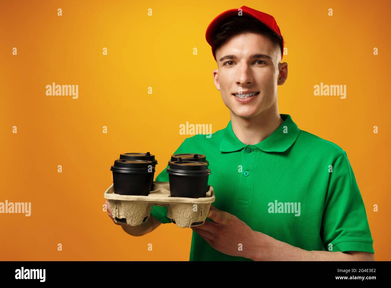 Young delivery man holding coffee cups against yellow background Stock ...