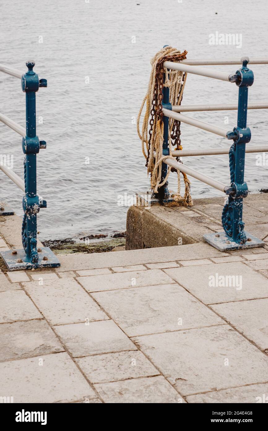 Seafront path with metal barriers, weathered rope and chain looking ...