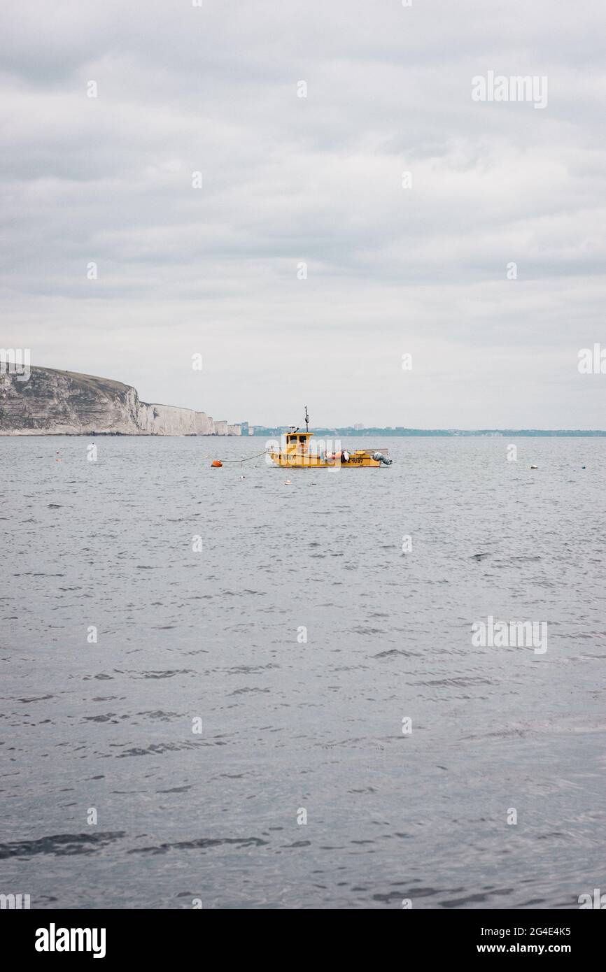Single yellow fishing boat moored in Swanage harbour on a cloudy day ...