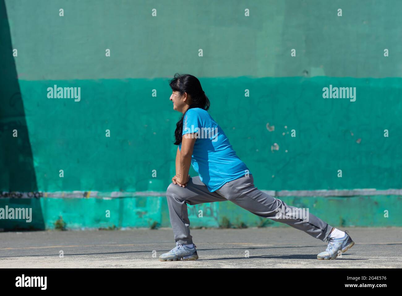 A side view of an aged Mexican female stretching the legs outdoors ...