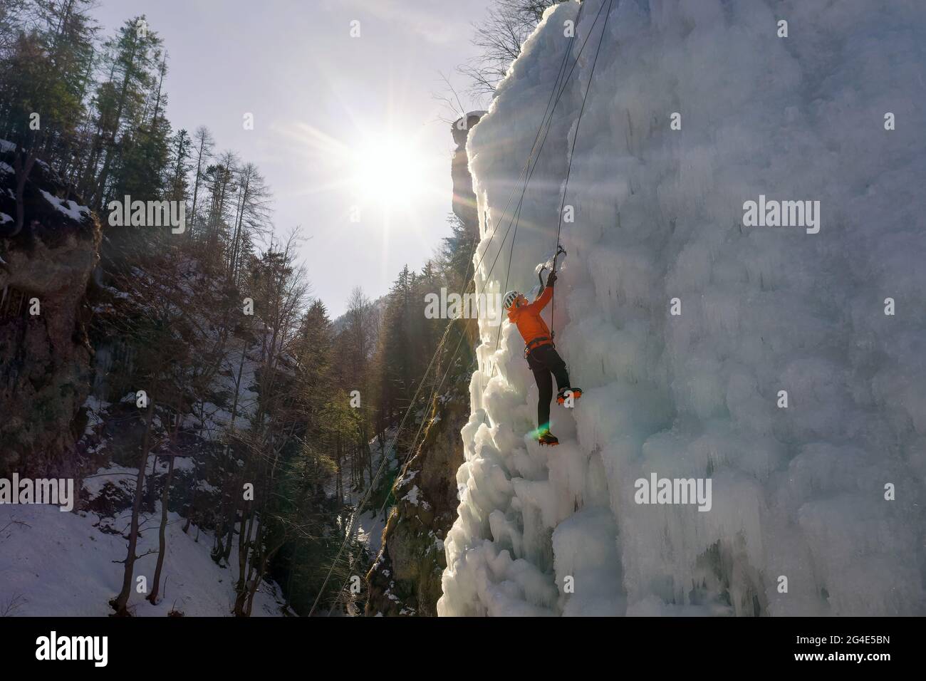 Aerial shot of an ice climber ascending the ice waterfall in the sun ...