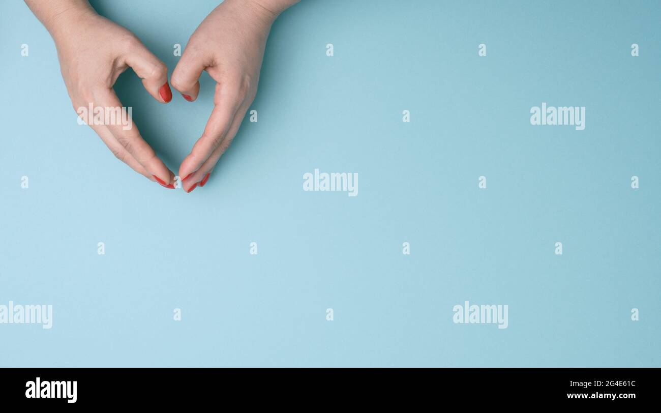 two female hands folded in the shape of a heart on a blue background ...