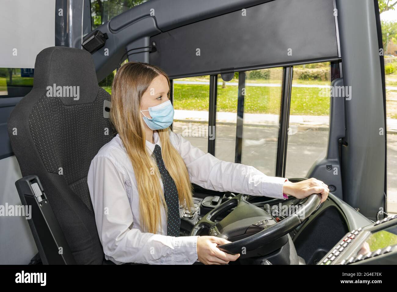 Young Caucasian female bus driver in a protective mask driving a bus ...