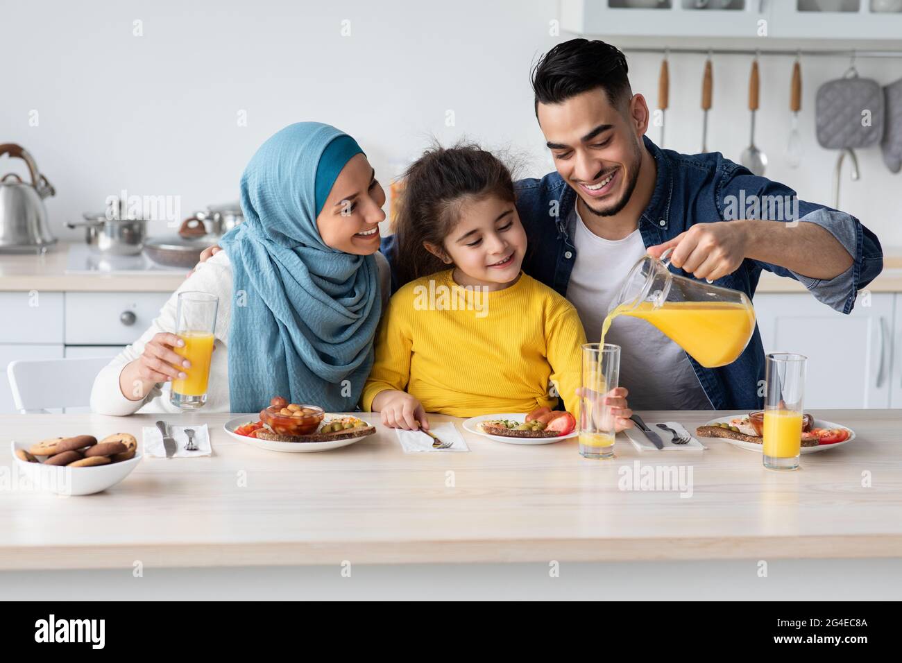 Happy Muslim Family Of Three Drinking Orange Juice During Breakfast In ...