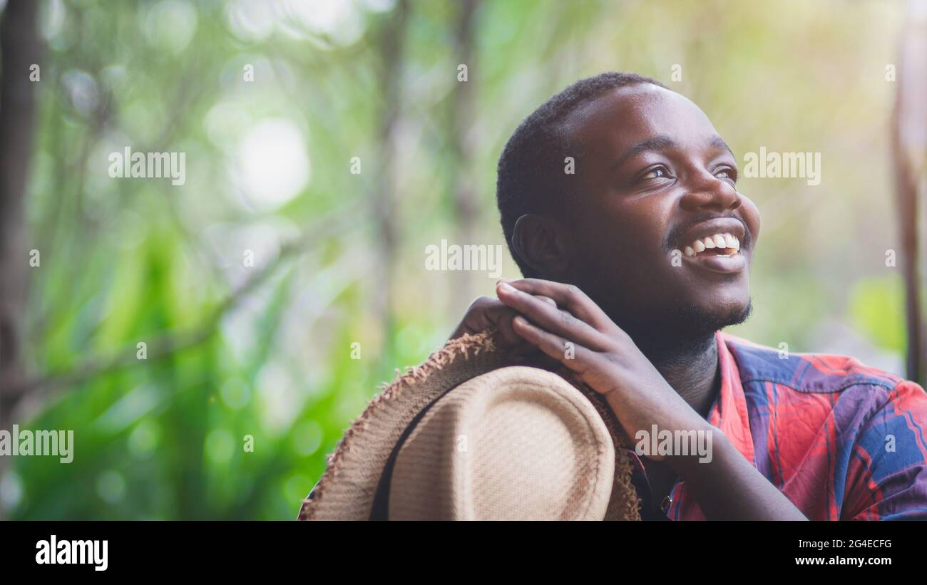 Happy african man smiling and holding hat with the green nature ...