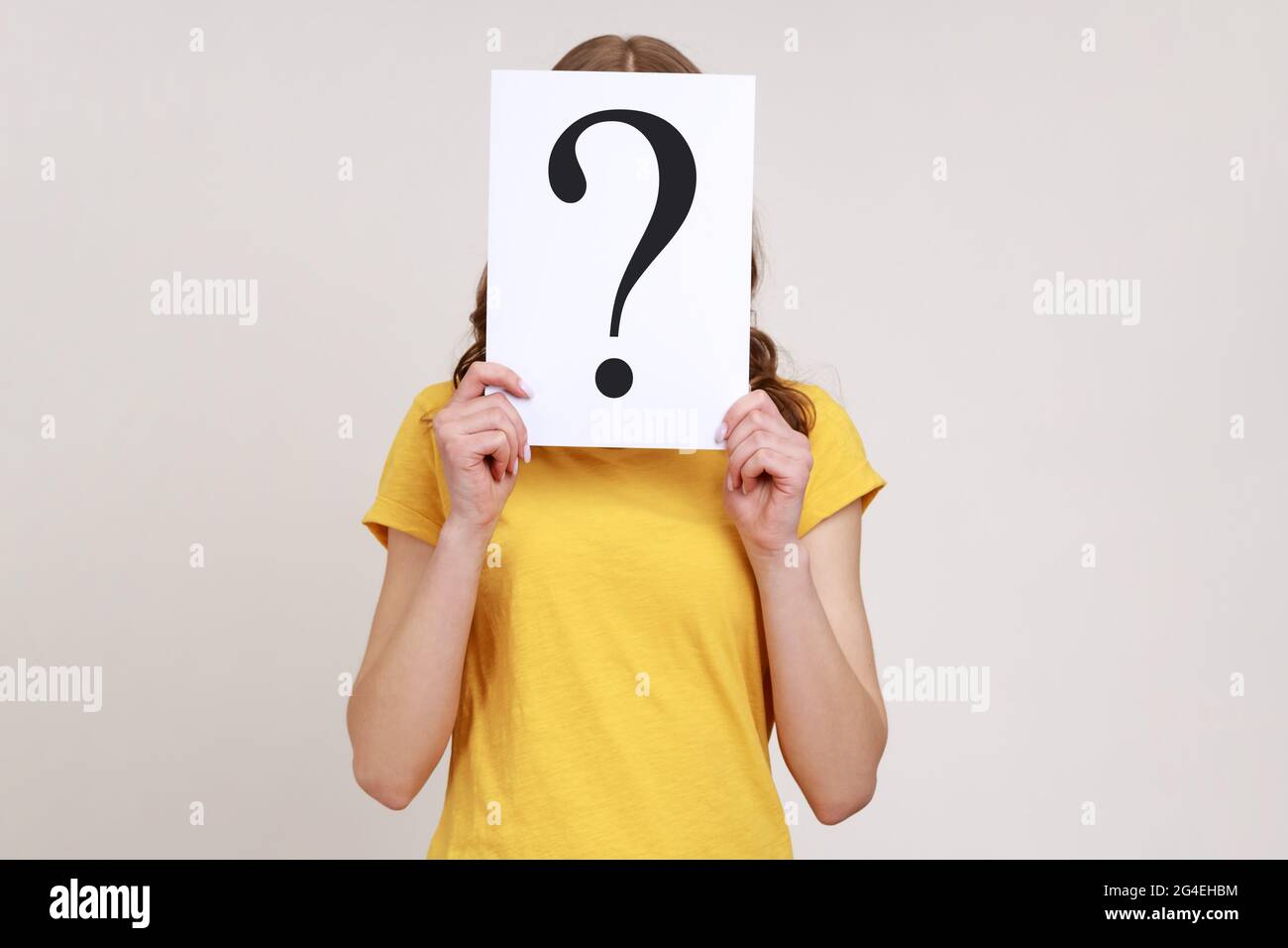 Portrait of shy woman in yellow casual T-shirt, hiding her face behind ...