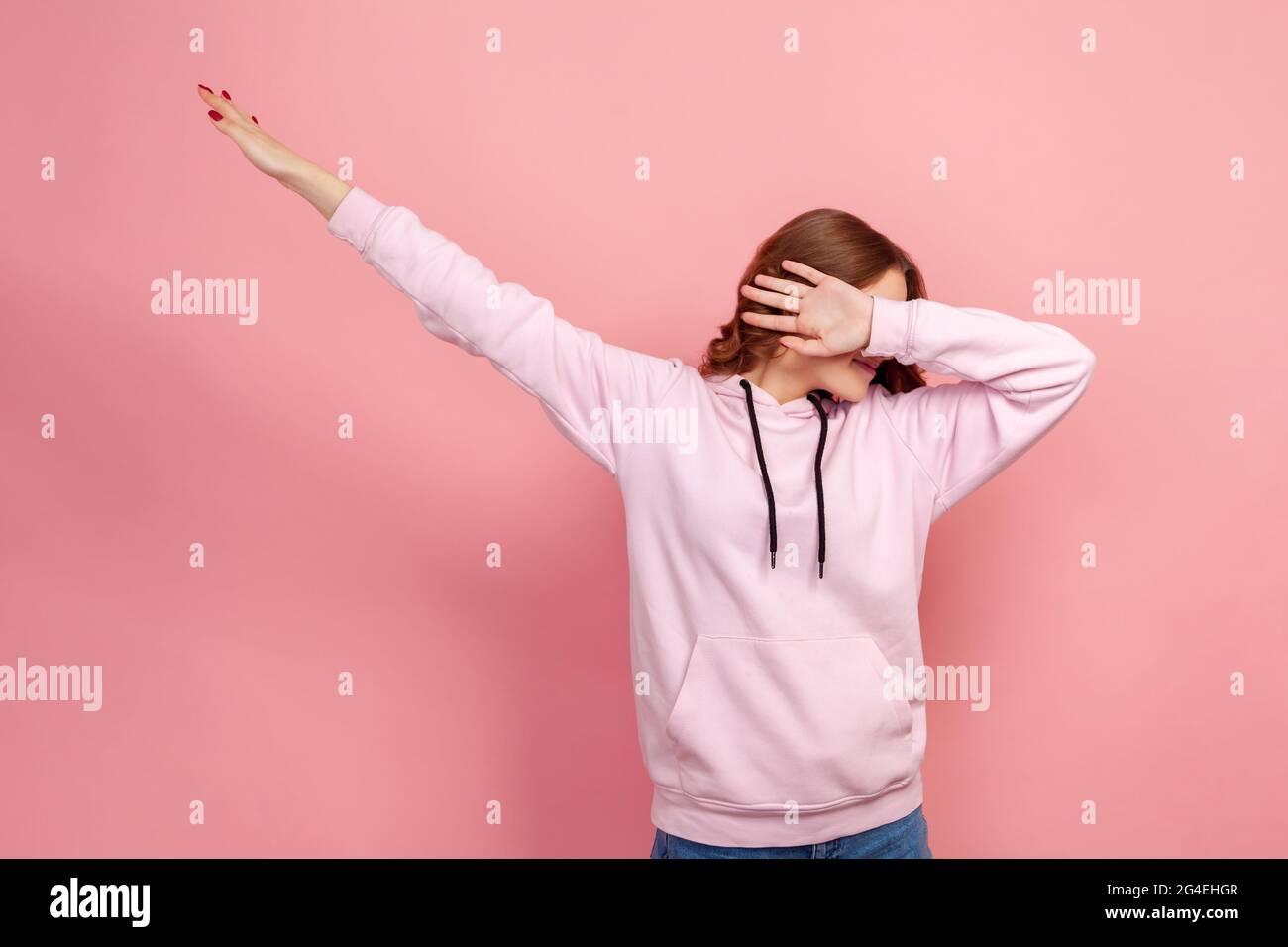Portrait of young female in hoodie raising hands in dab dance pose ...