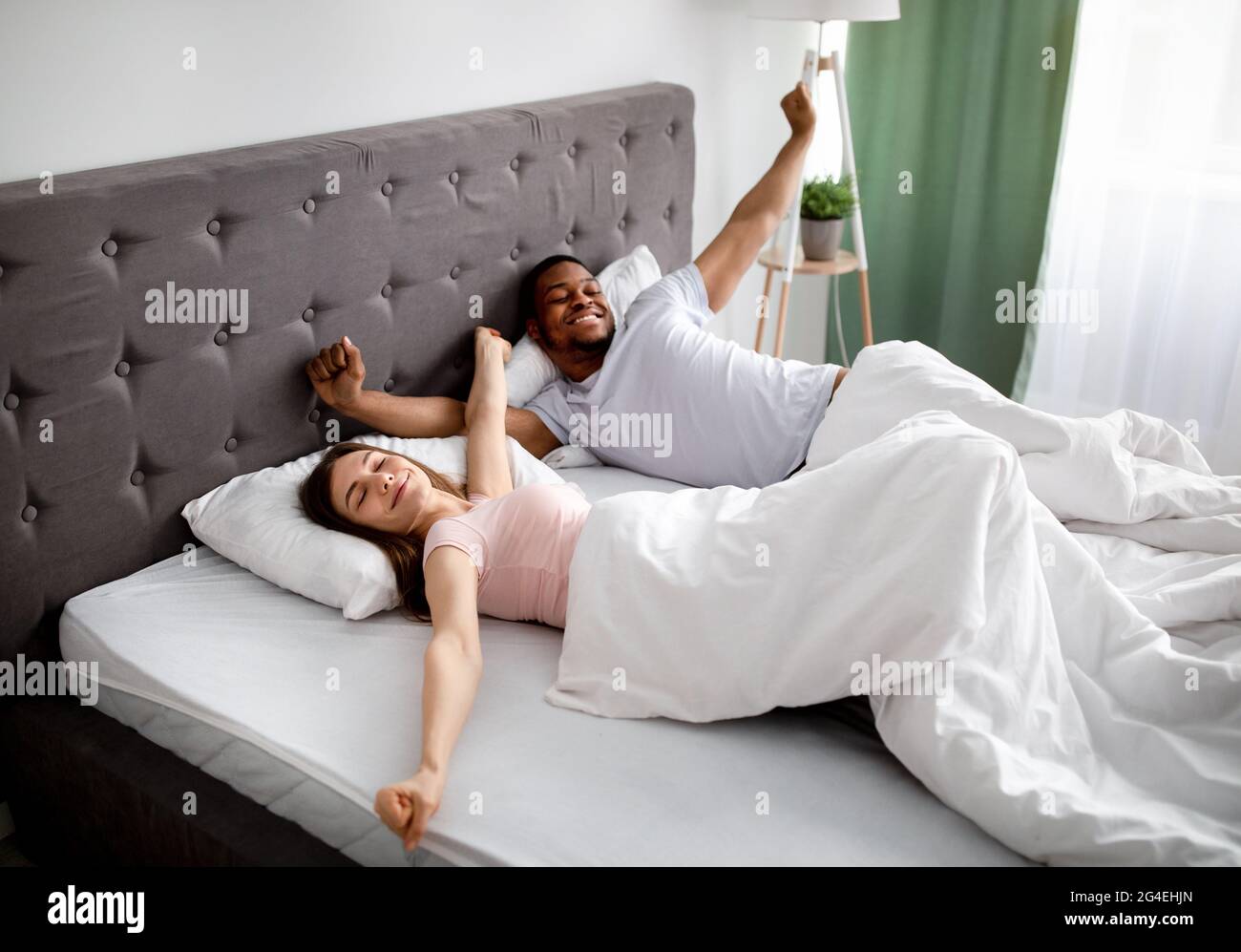 Millennial Multiethnic Couple Waking Up In Morning Stretching On Bed