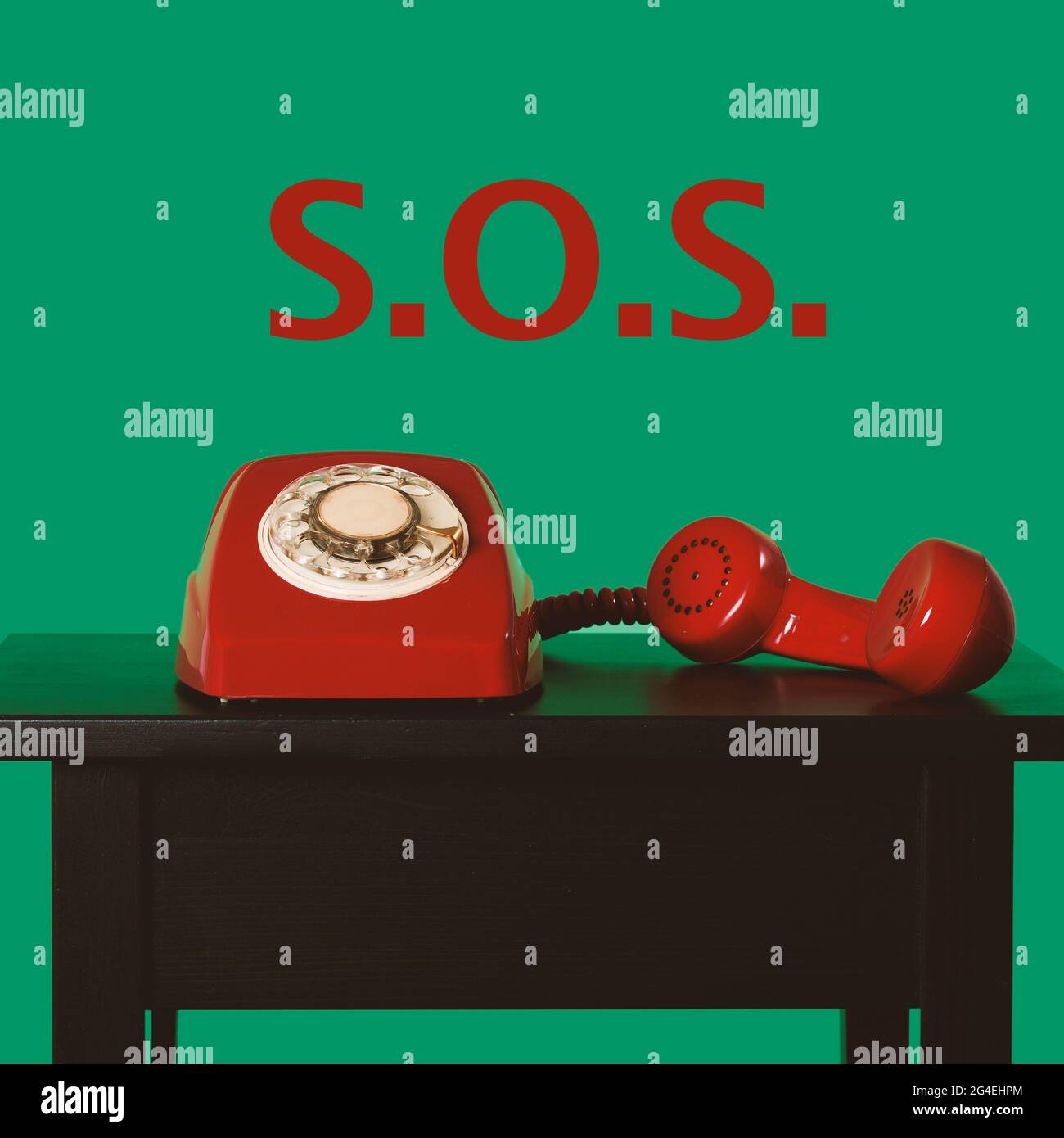 closeup of a red landline rotary dial telephone off-the-hook on a table ...