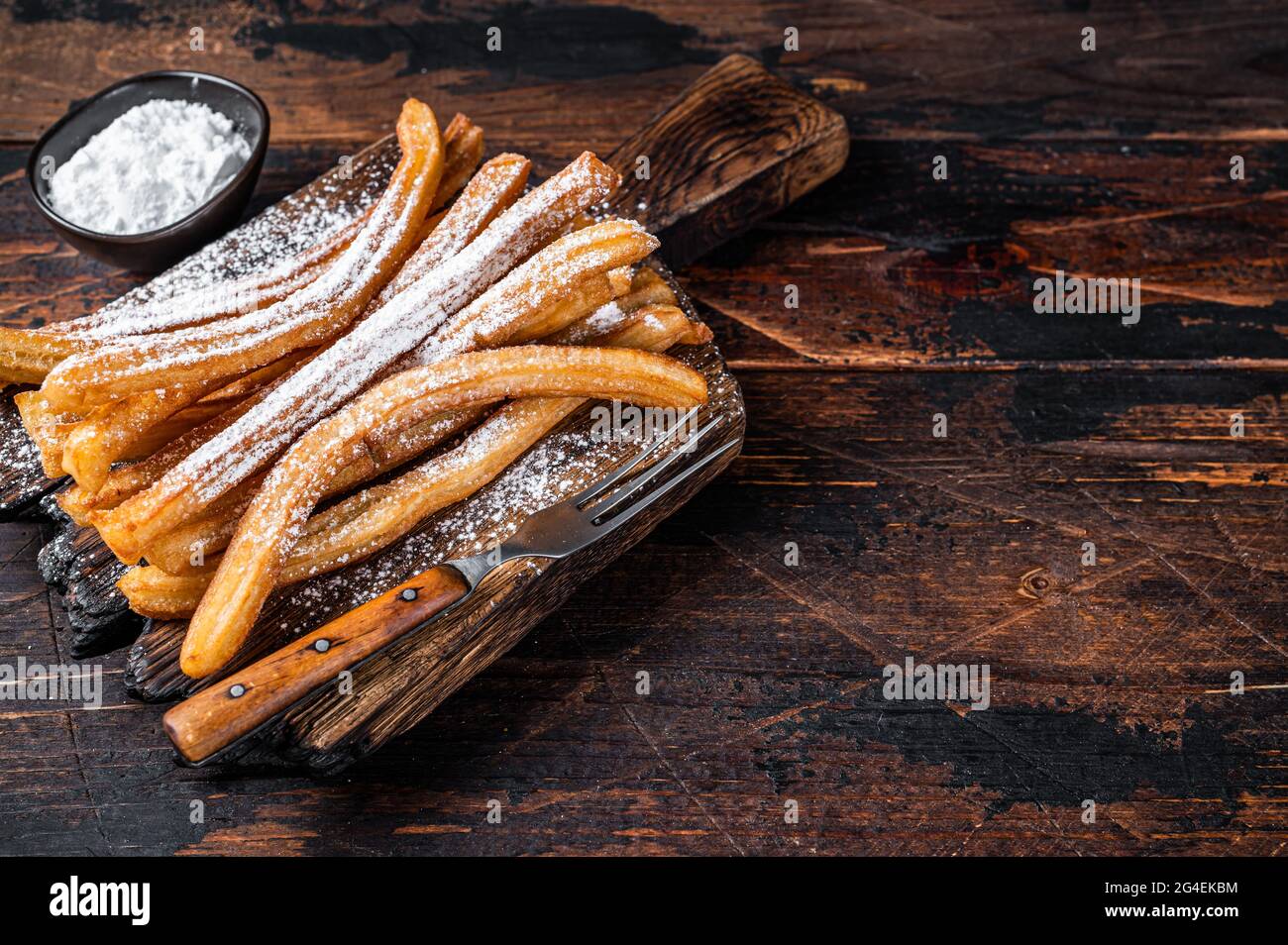 Spanish dessert churros with sugar powder on a wooden tray. Dark wooden ...