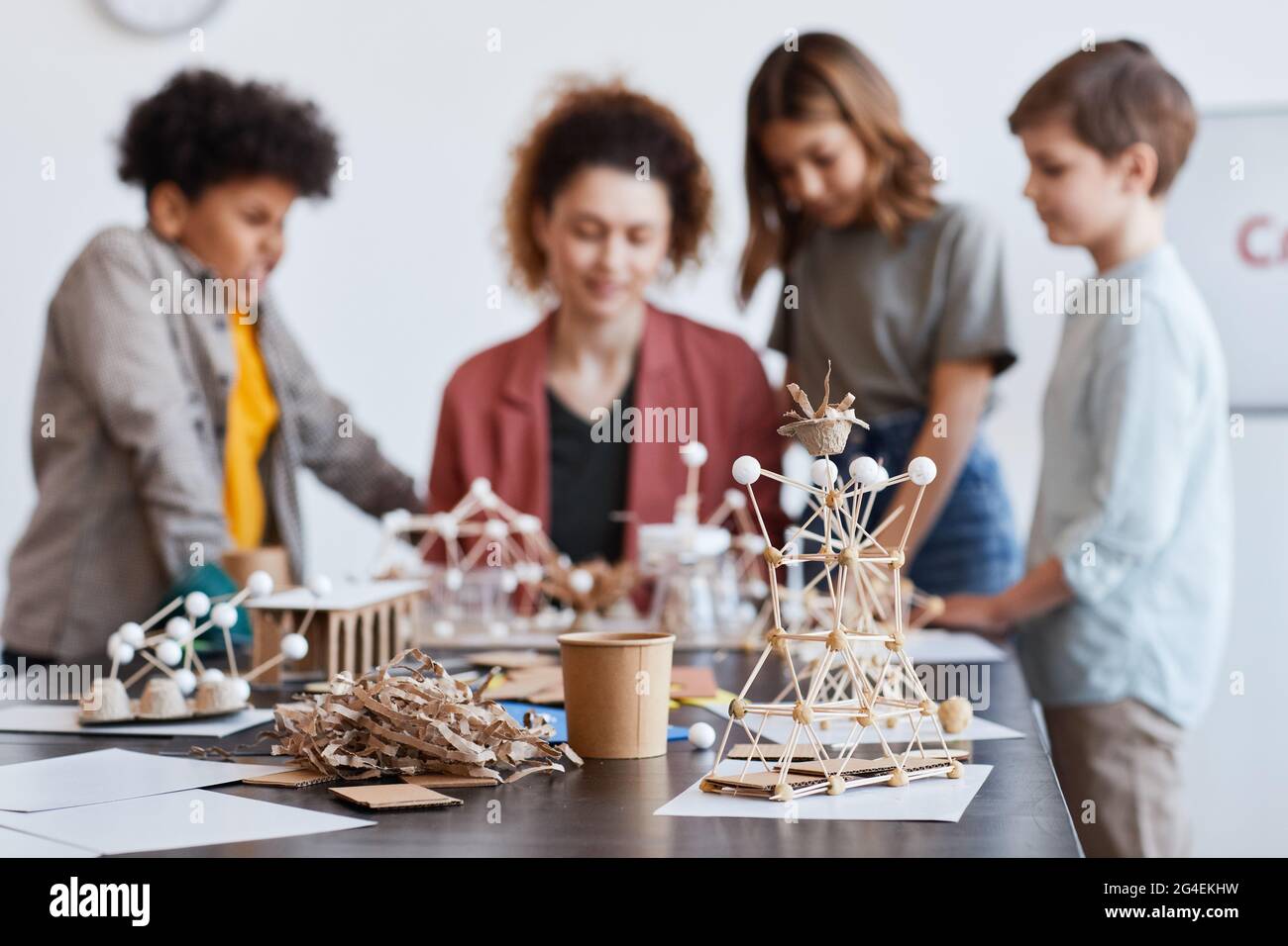 Female teacher helping children making wooden models during art and ...