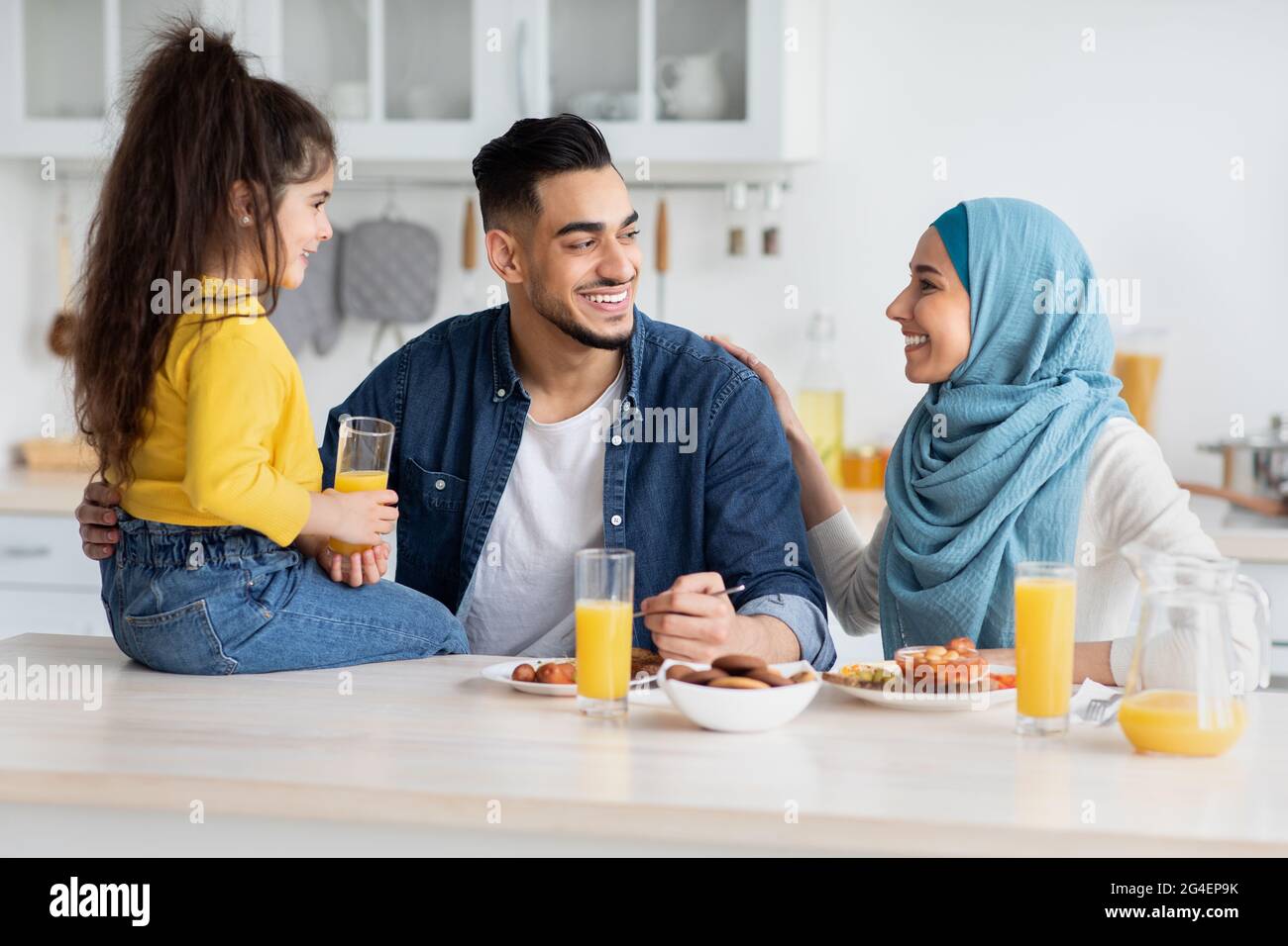 Cheerful Muslim family Of Three Having Breakfast In Kitchen, Chatting ...