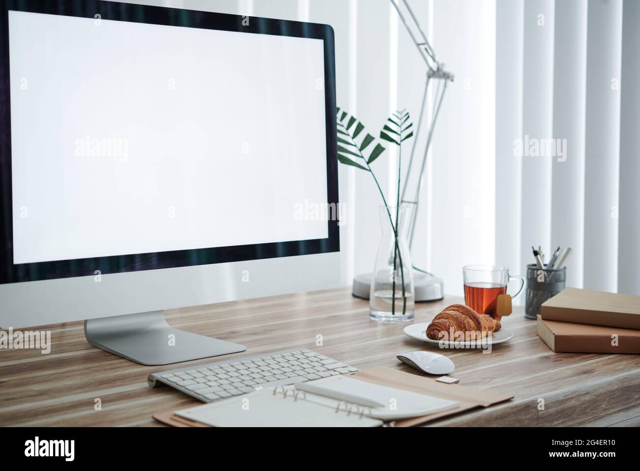 Empty computer monitor, opened planner, croissant on plate and stack of ...