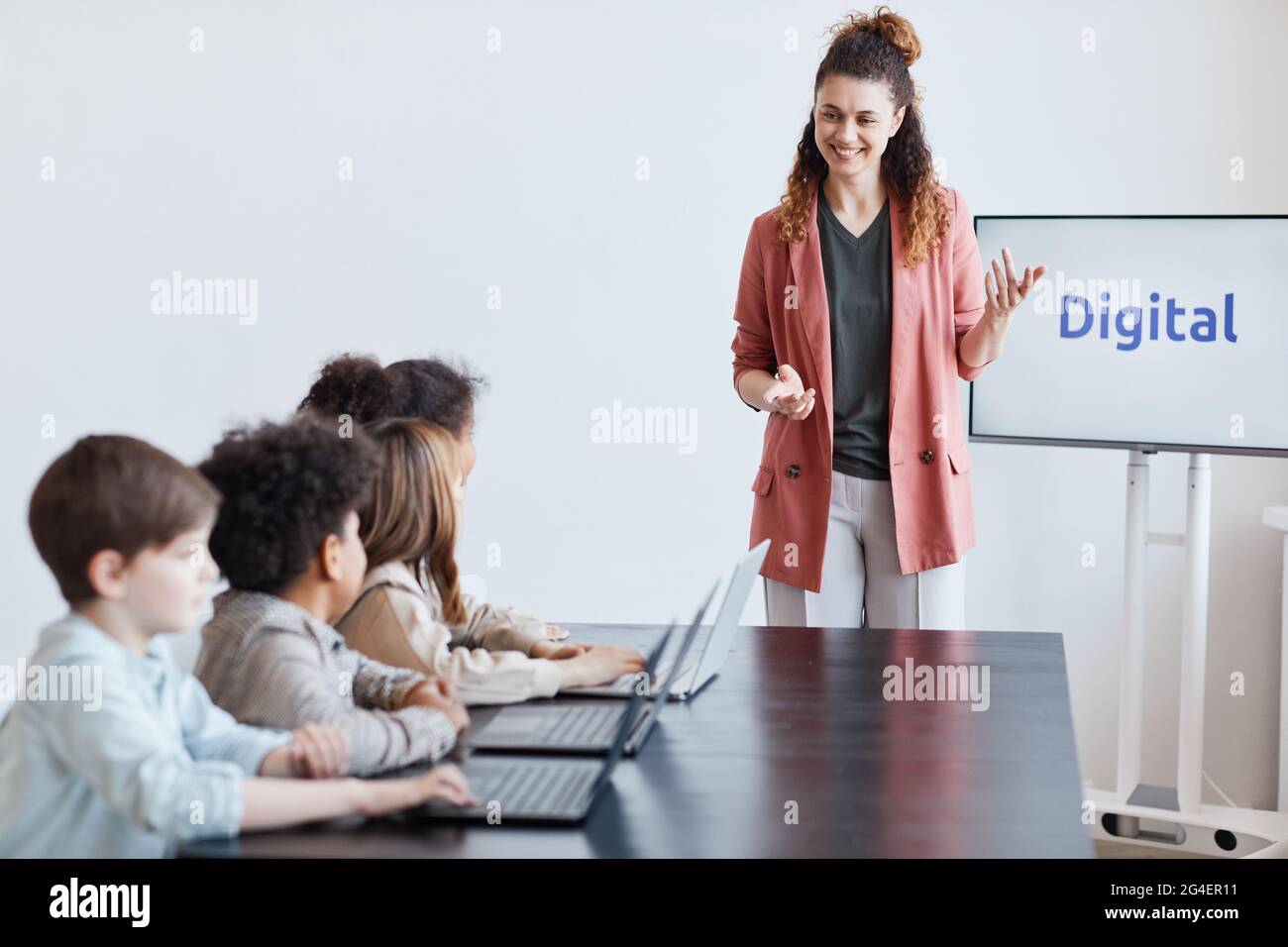 Portrait of smiling female teacher talking to group of kids using ...
