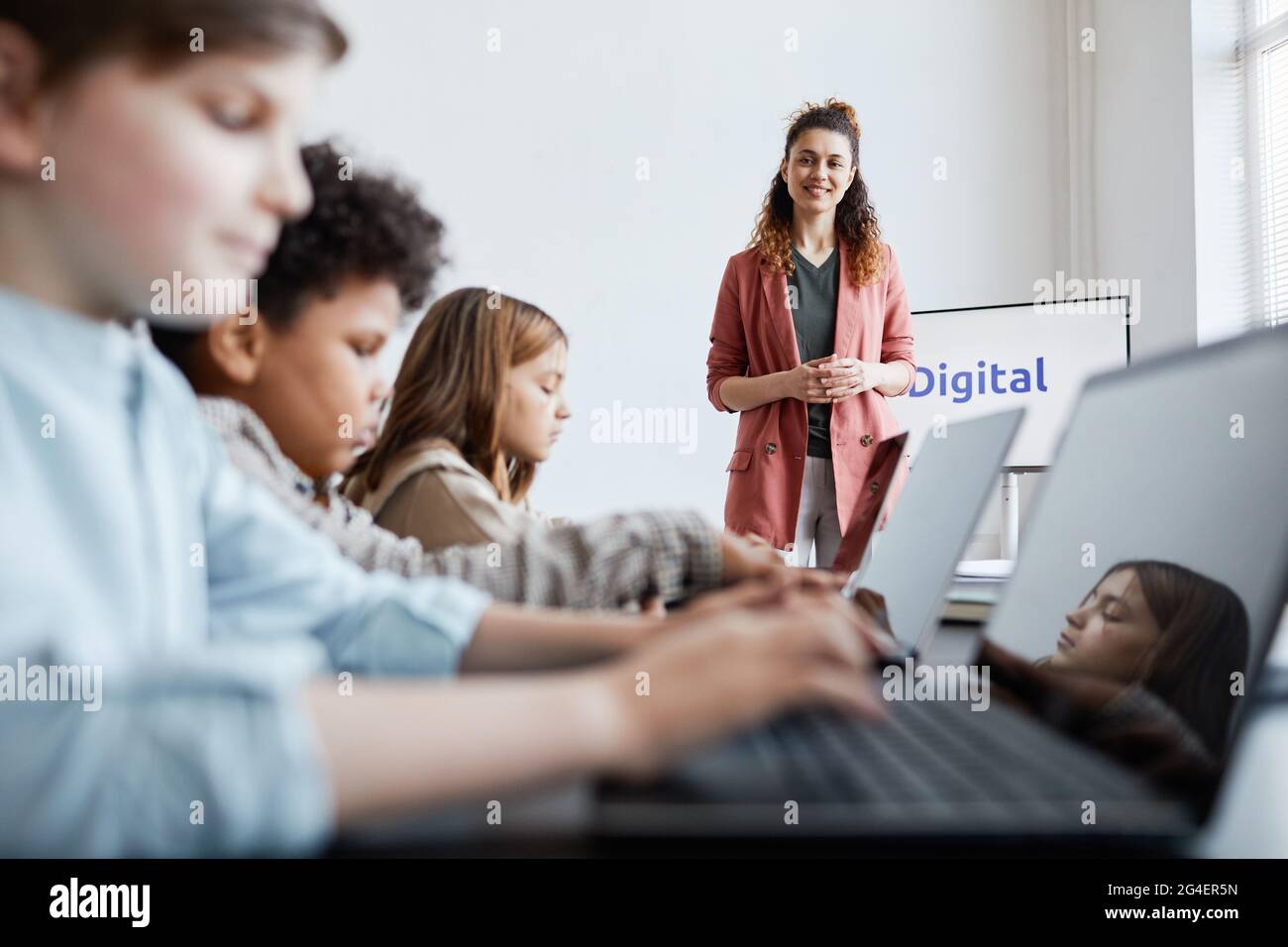 Portrait of smiling female teacher with group of kids using computers ...