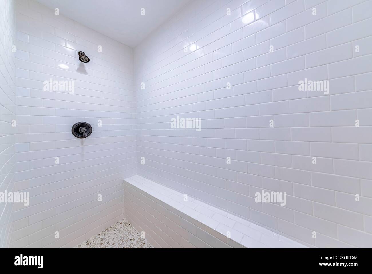 A white-tiled shower area with a sitting space Stock Photo - Alamy