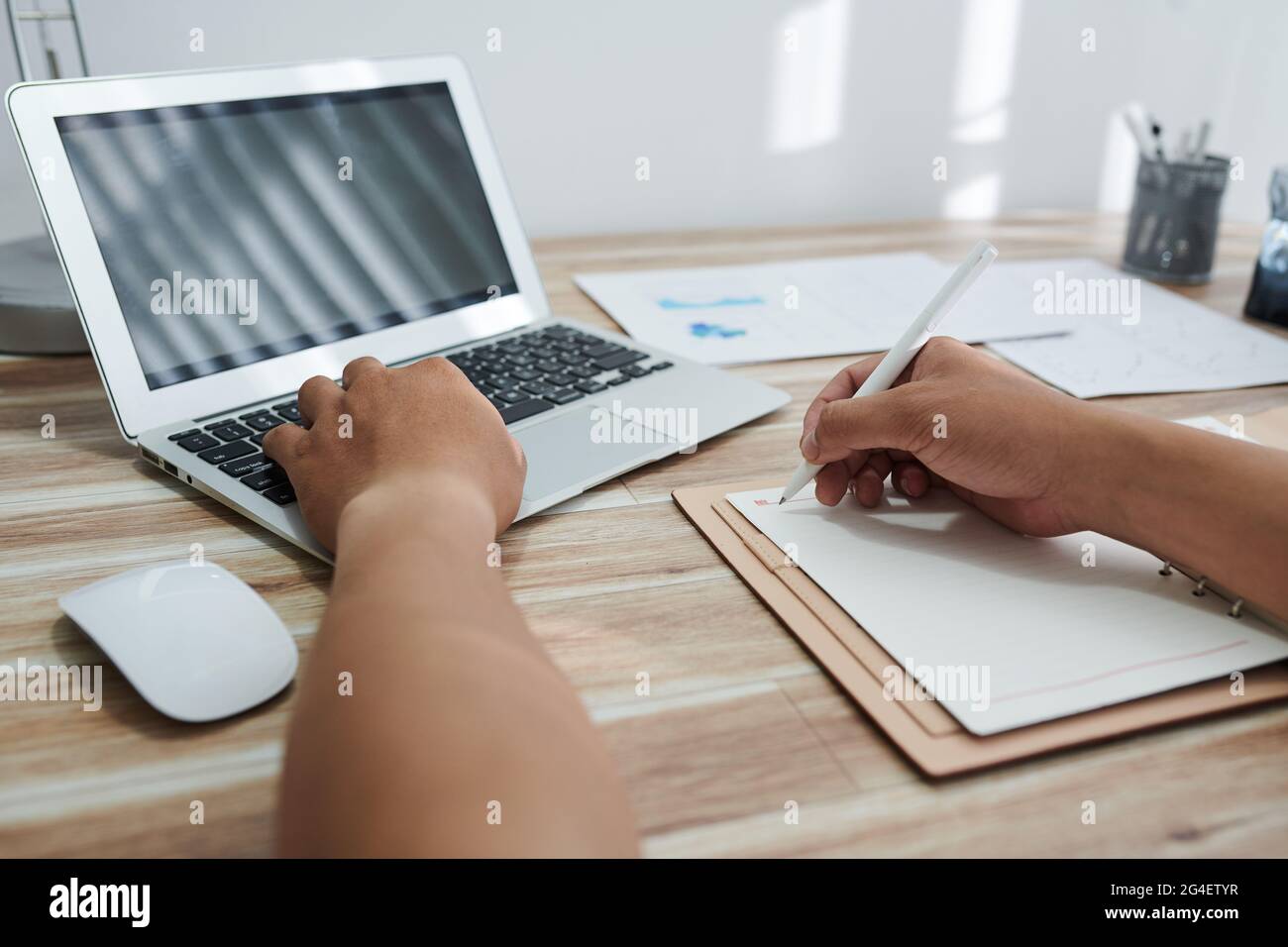 Hands of student reading article on laptop screen and taking notes in ...