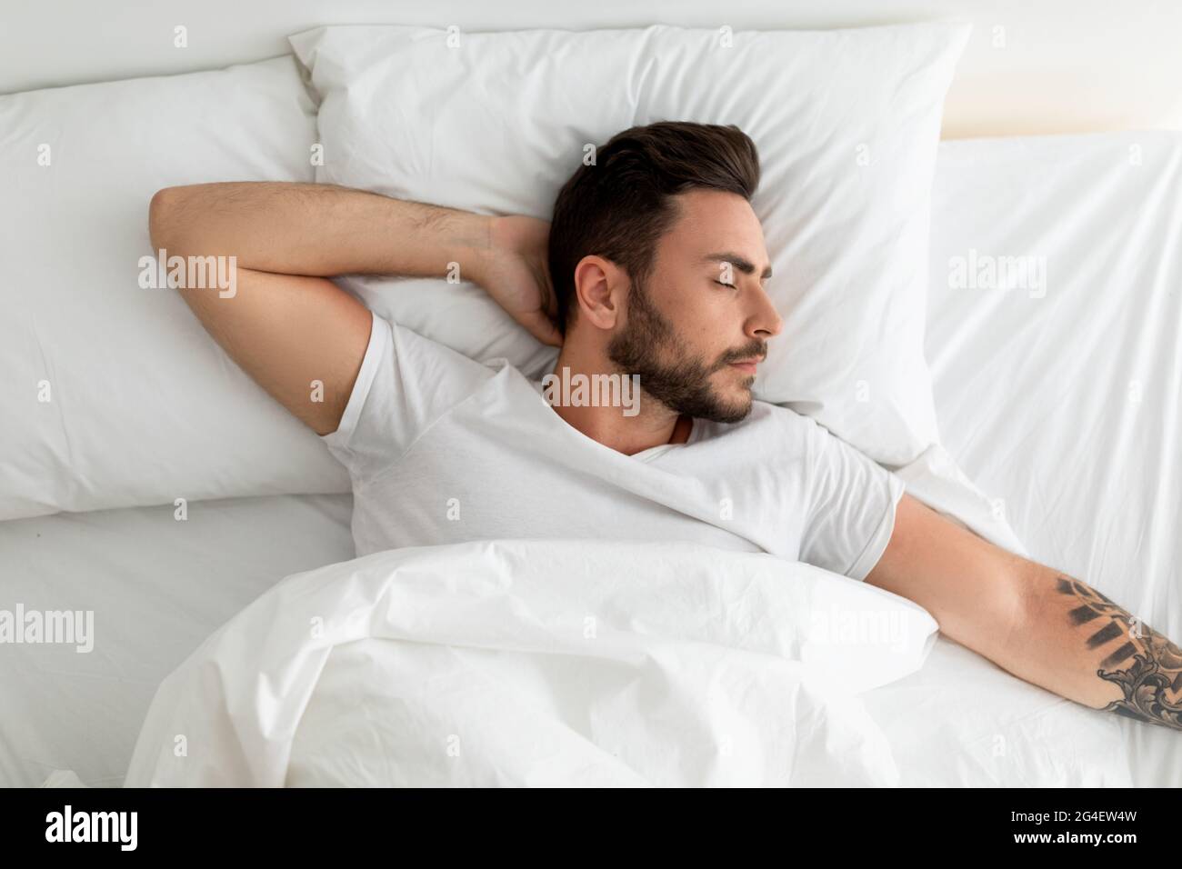 Tired millennial man sleeping, lying on white bed in bedroom, resting ...