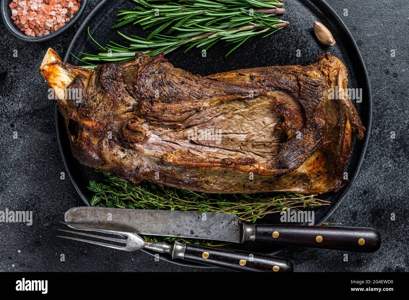 Roasted lamb mutton shoulder meat on a plate with knife and fork. Black ...