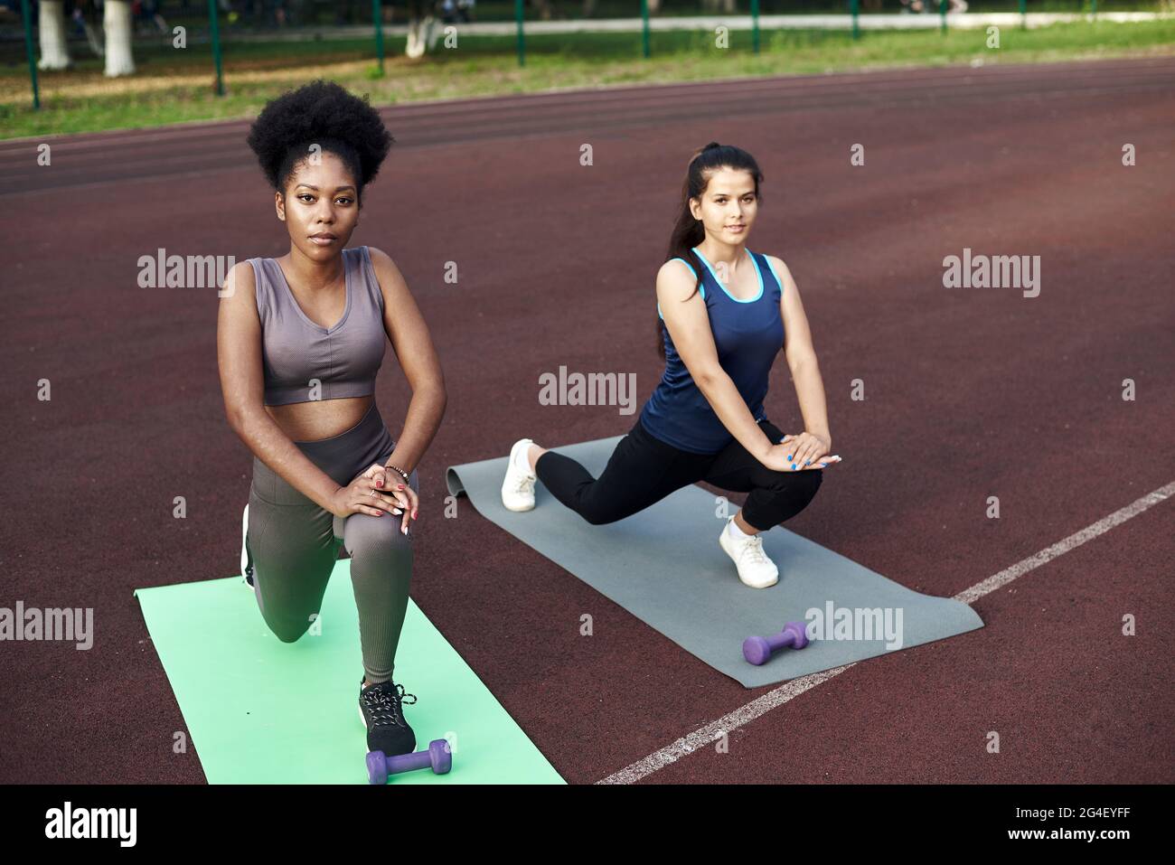 Two fit smiling young woman working out together in a park doing ...