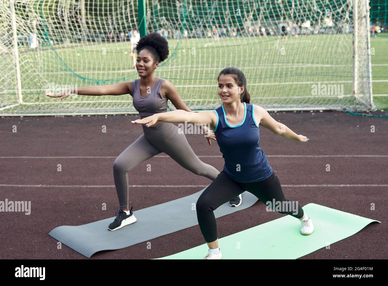 Two fit smiling young woman working out together in a park doing ...