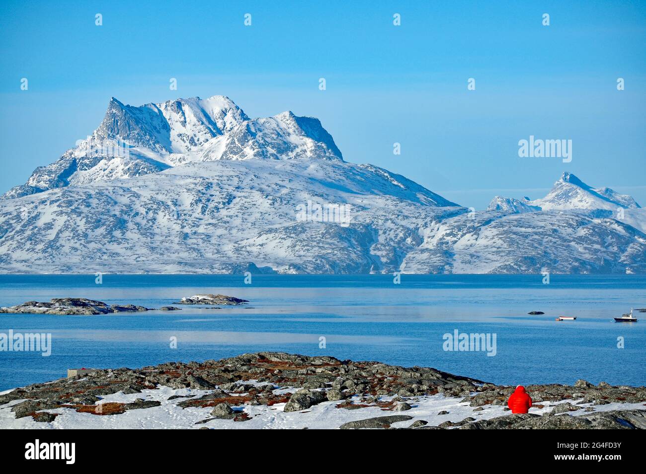 Man with red jacket in front of fjord and mountains with snow, evening ...