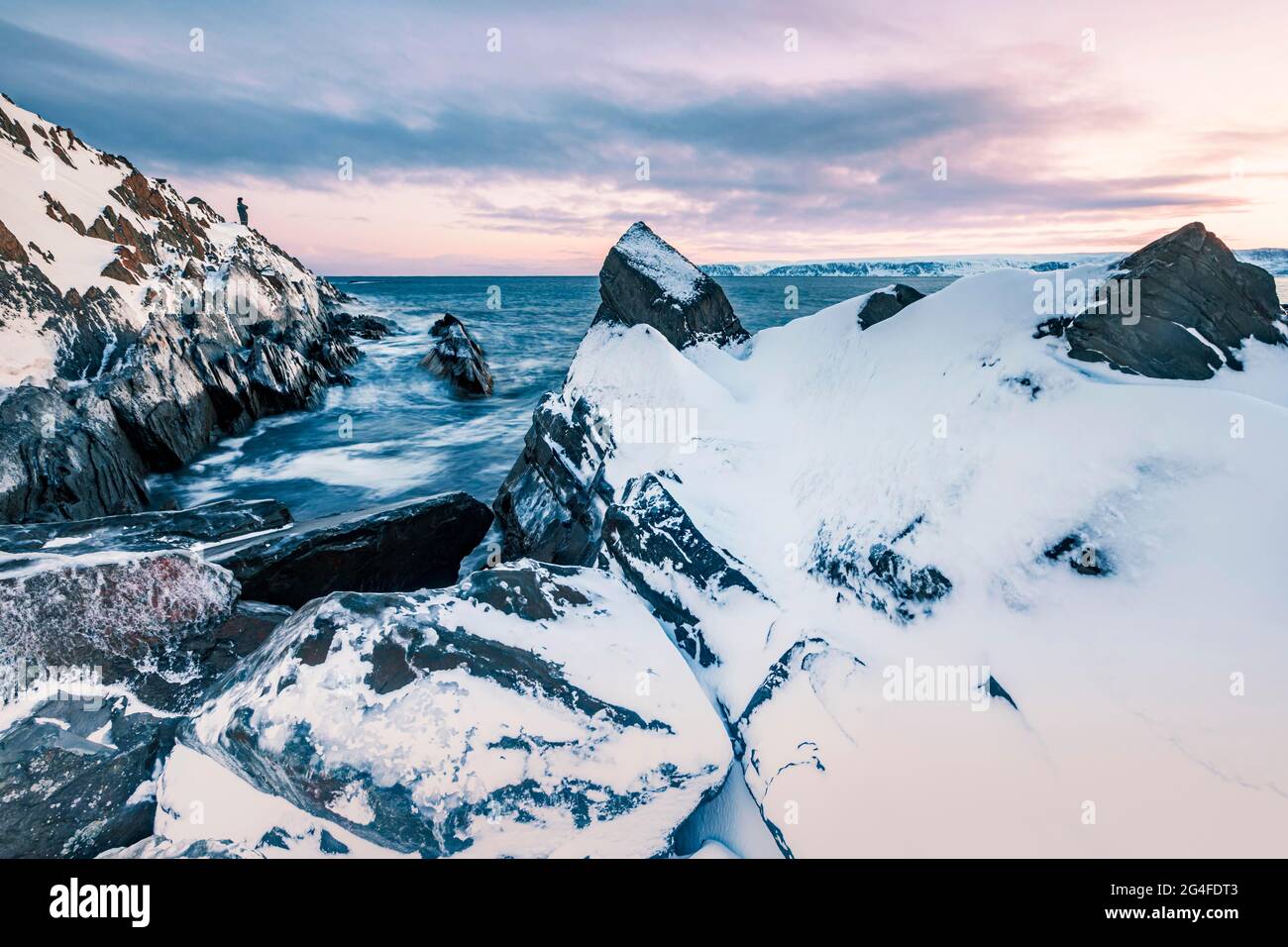 Man standing on cliff, coastal landscape in winter, Berlevag, Norway ...
