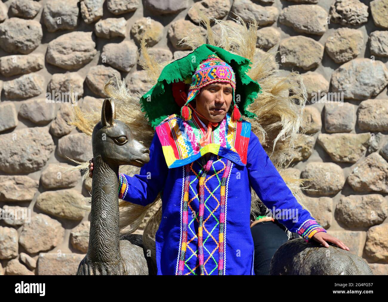 Indigenous man in colorful traditional costume in front of an Inca wall ...