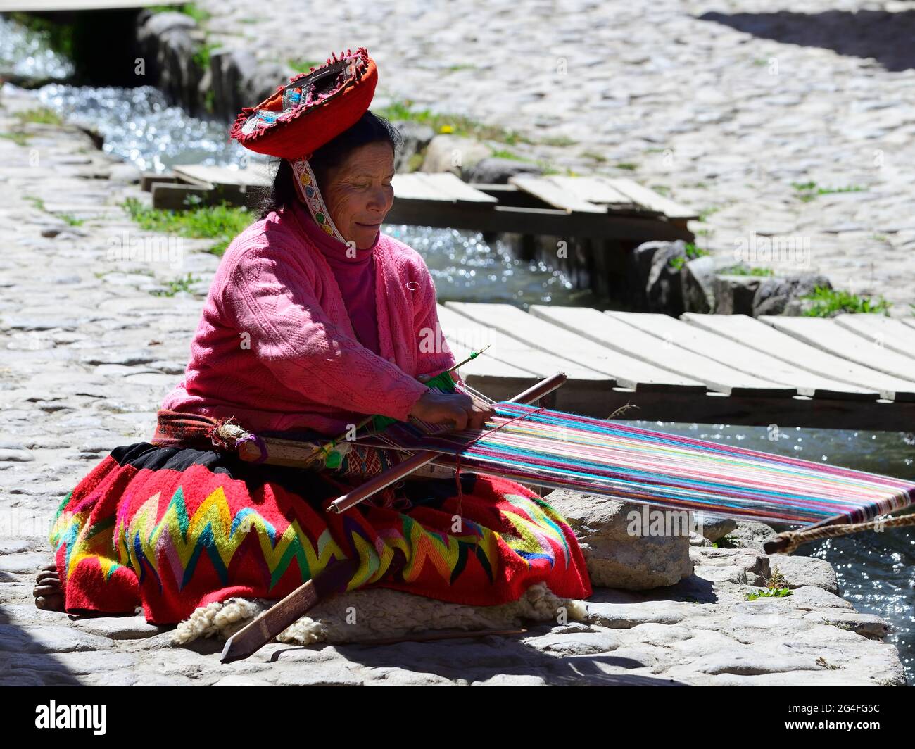 Indigenous woman sitting on paved path weaving, Ollantaytambo, Cusco ...