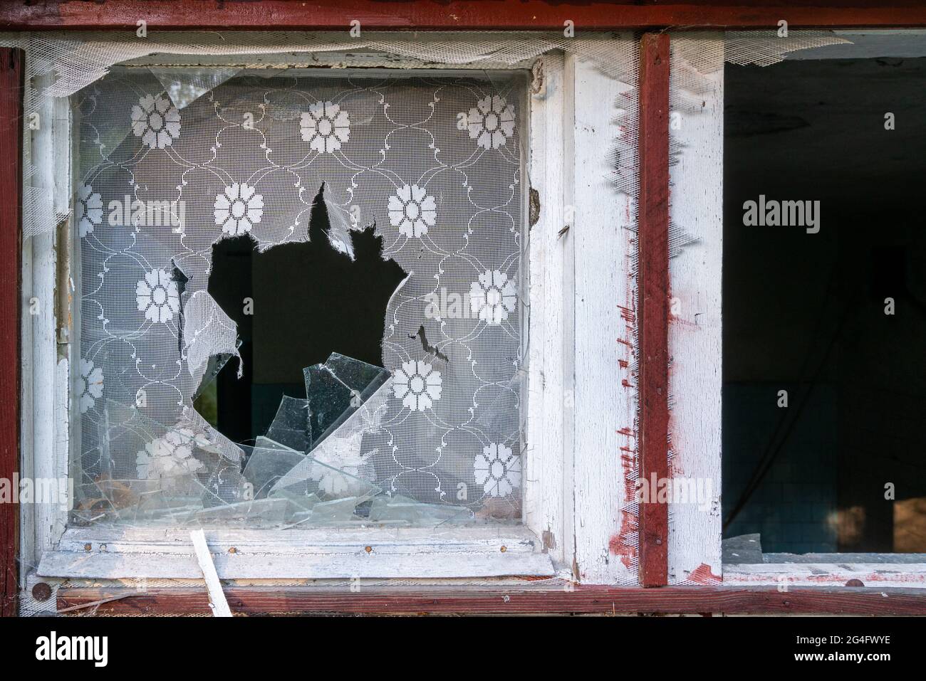 Small broken window with red frame and window shades torn apart. Detail ...