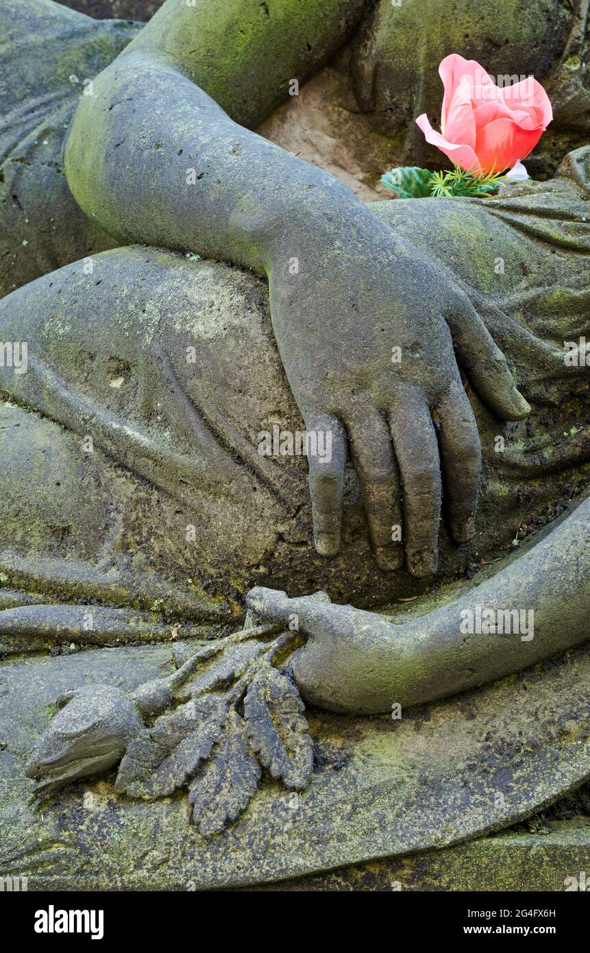 Mourning statue of mother and dying child, close-up with hands and pink ...