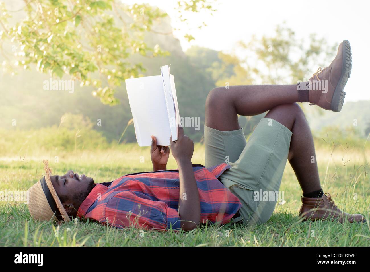 African man reading a book on the grass happily on vacation Stock Photo ...