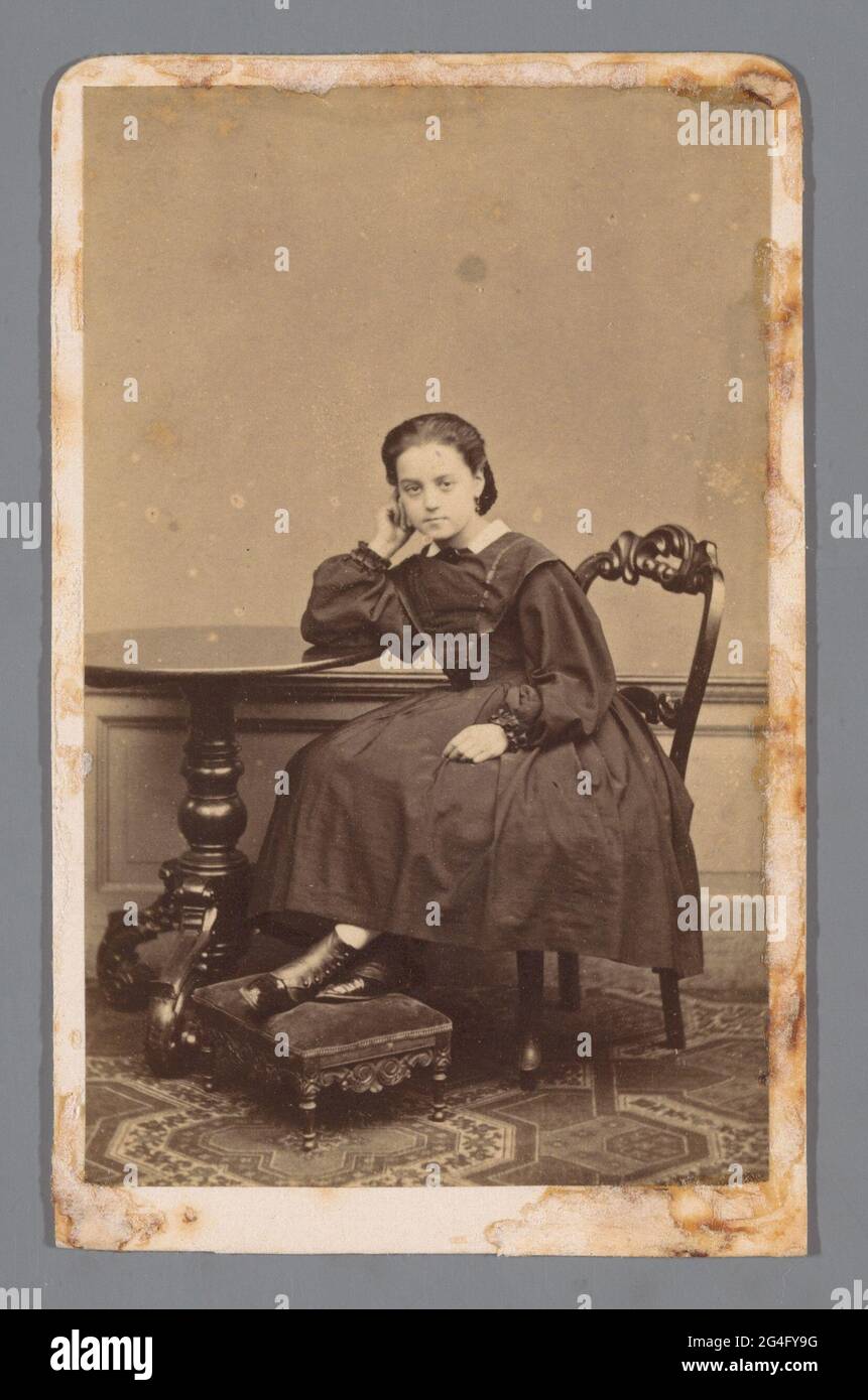 Portrait of a young girl. Young girl in dark dress, sitting at small ...