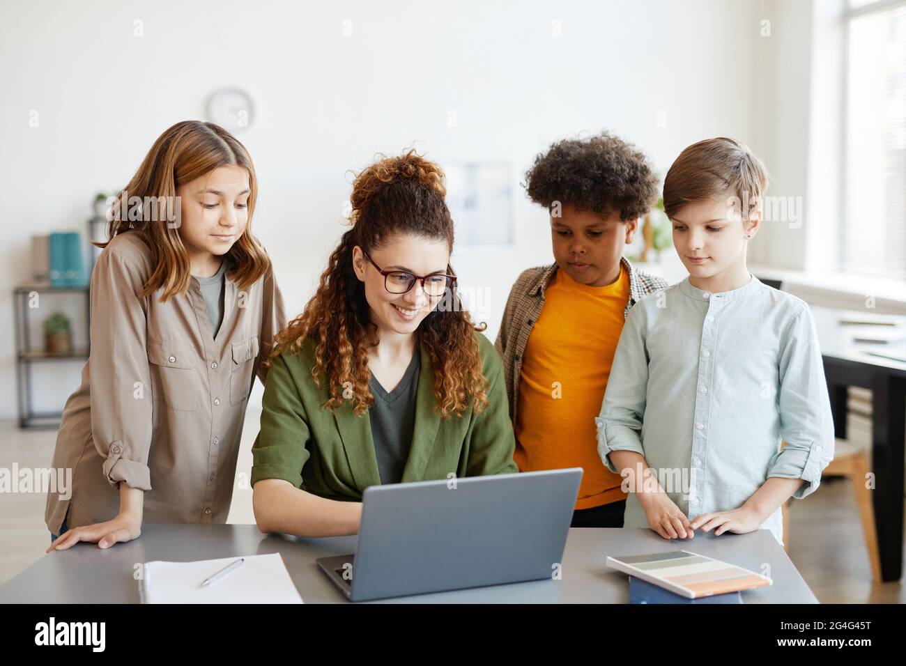 Portrait of young female teacher using computer with diverse group of ...