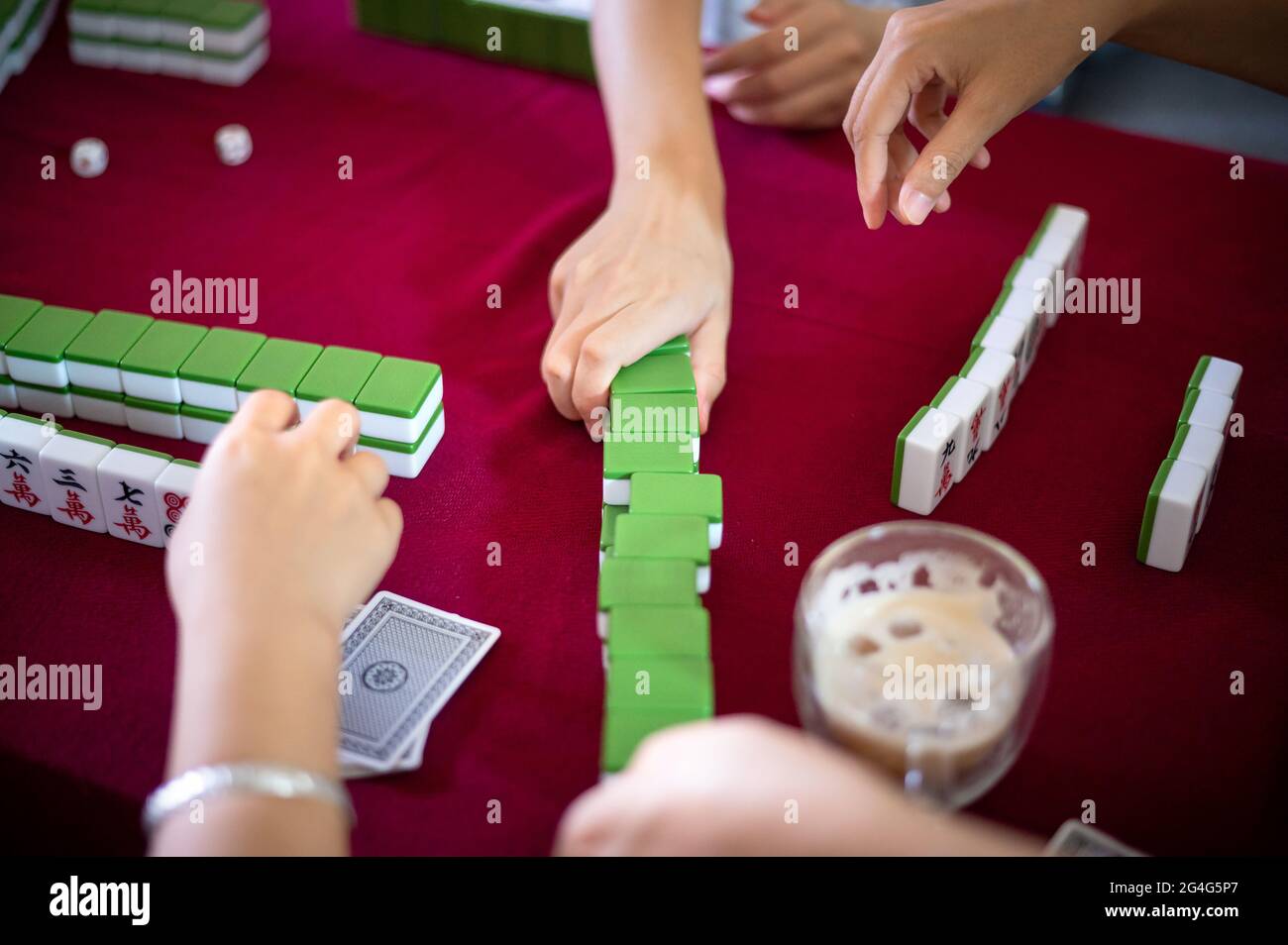 People playing mahjong traditional Chinese board game on a red table at ...