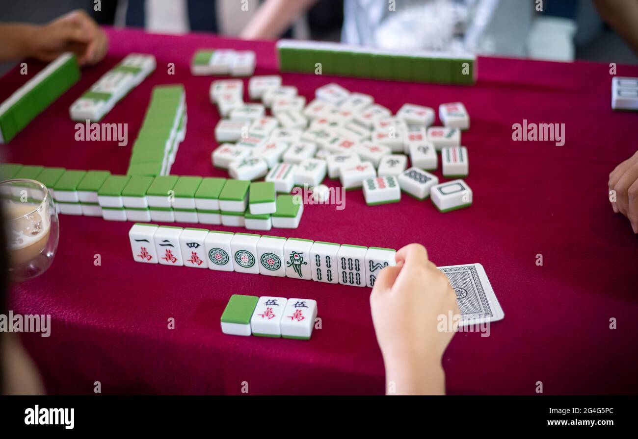 People playing mahjong traditional Chinese board game on a red table at ...