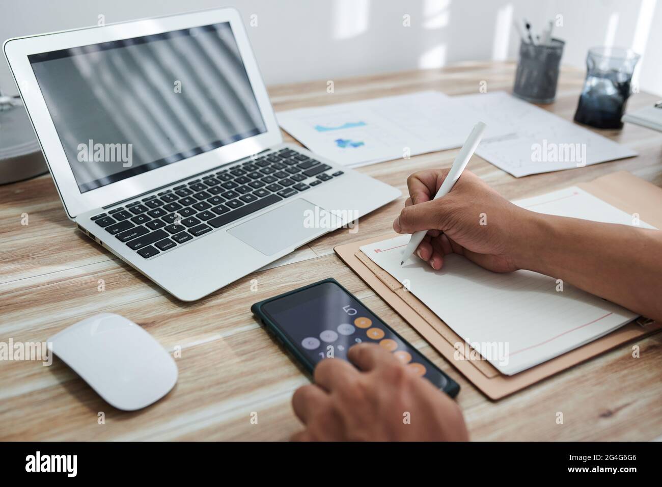 Hands of manager making calculations on smartphone and taking notes in ...